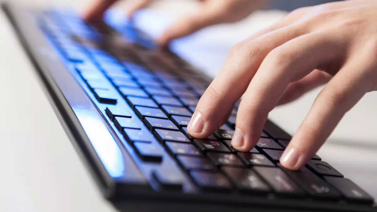 一個人的手在藍色背光鍵盤上打字