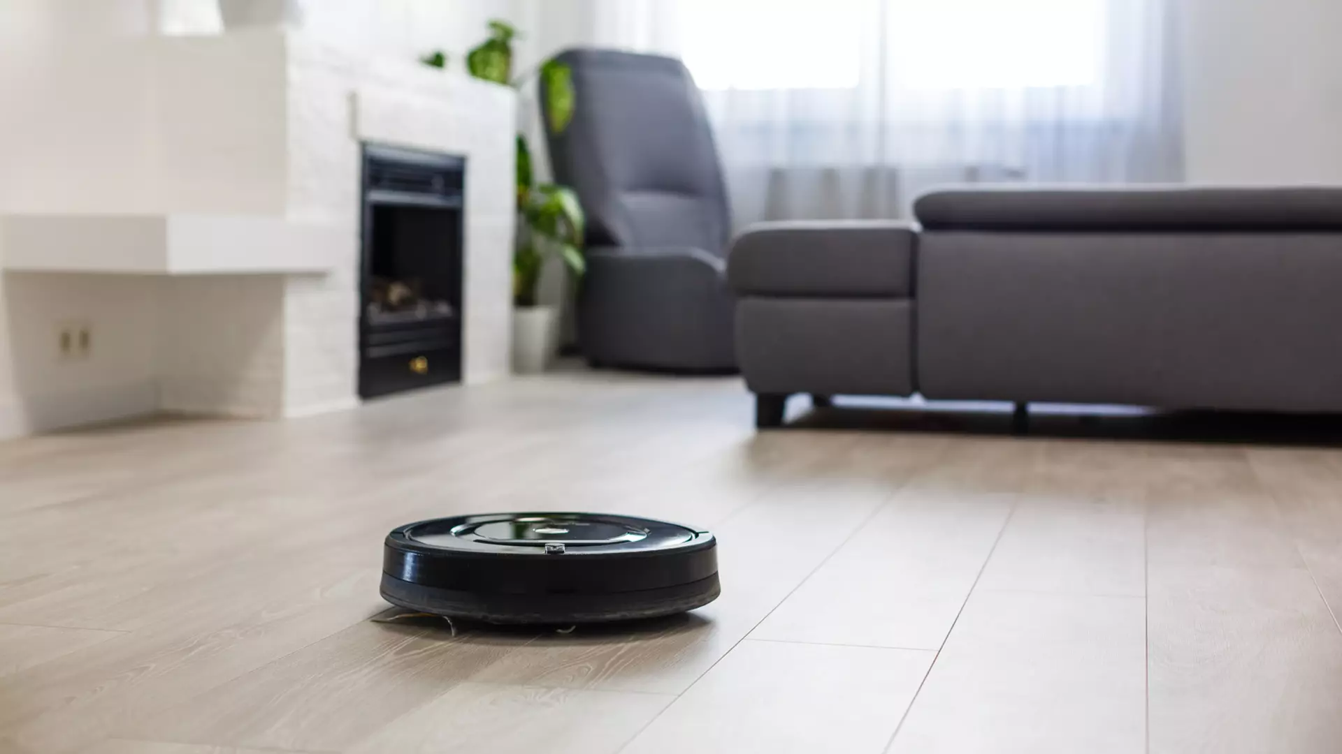 लिविंग रूम में लैमिनेट लकड़ी के फर्श पर रोबोटिक वैक्यूम क्लीनर