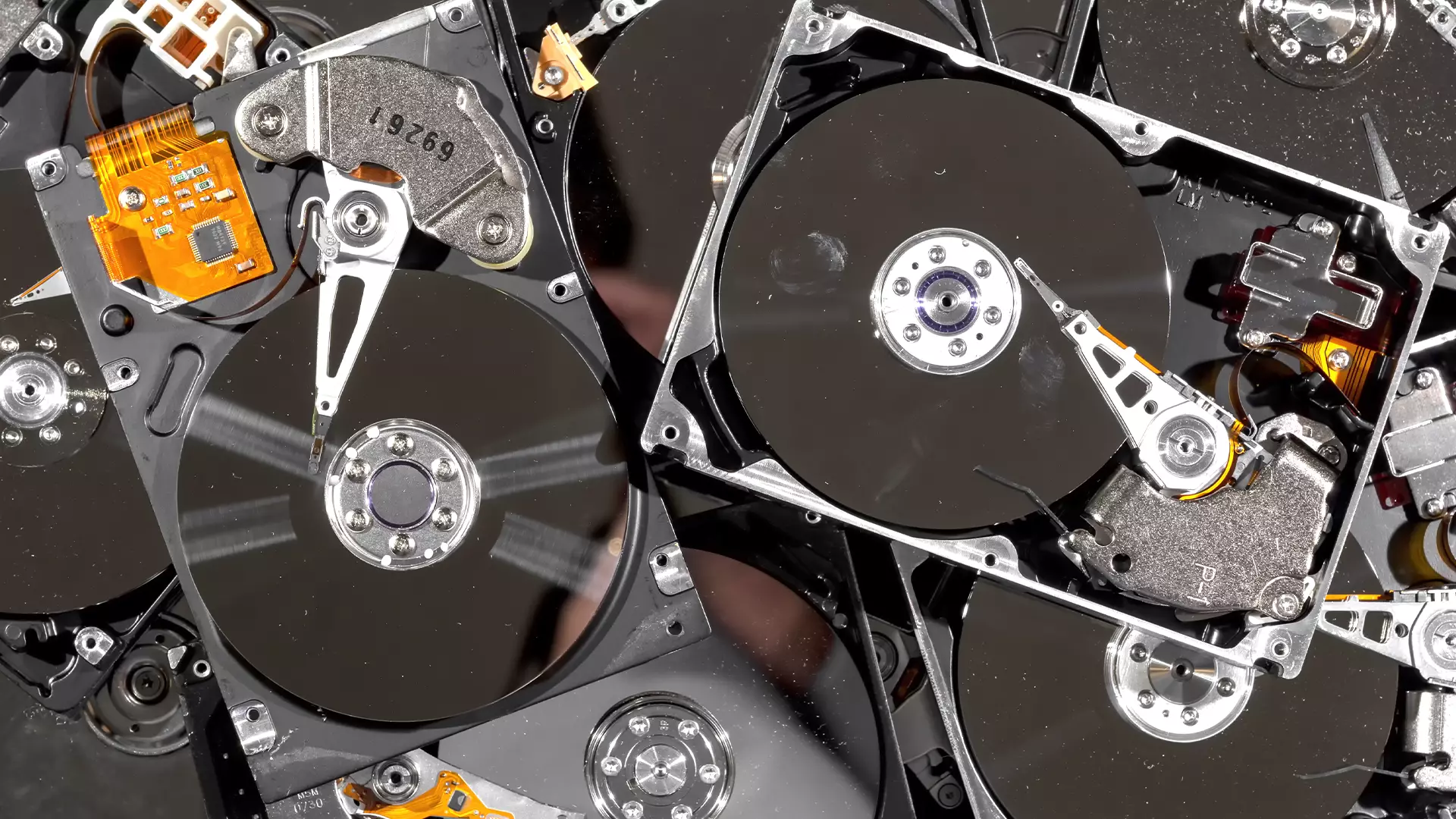 Hromada pevných disků s odkrytými disky. Všude na jednotkách je nepříjemný prach a otisky prstů.