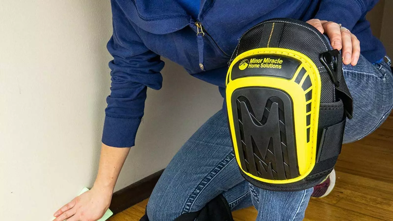 En person på ett kne, iført de gule og svarte Minor Miracle Home Solutions knebeskyttere.