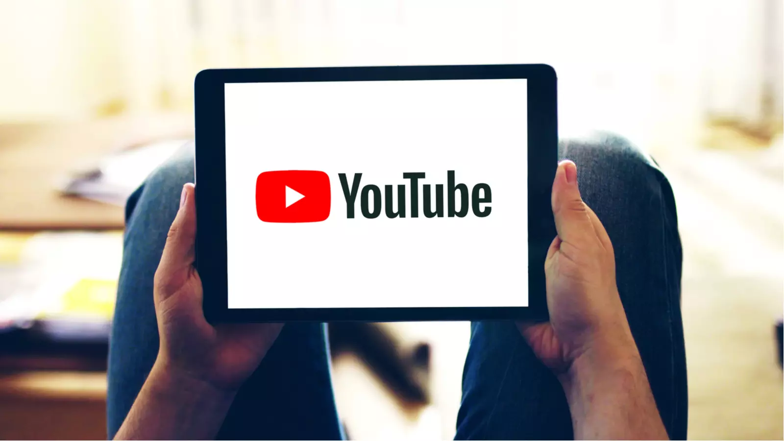 Logo de l'application YouTube sur un écran de tablette, mise au point sélective sur les mains d'une personne tenant un appareil mobile tout en regardant des vidéos en ligne à la maison