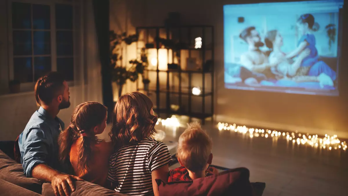 keluarga ibu bapa dan anak-anak menonton filem TV projektor dengan popcorn pada waktu petang di rumah