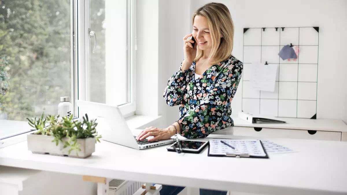 Forretningskvinne bruker telefonen mens hun jobber ved ergonomisk stående skrivebord