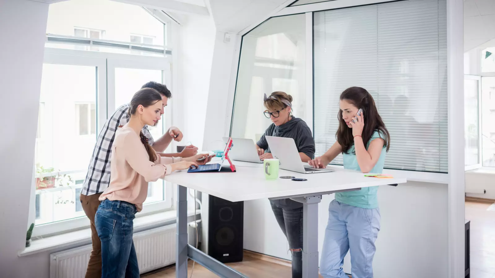 Заети колеги, използващи мобилни технологии, докато споделят изправено бюро в модерно офис пространство