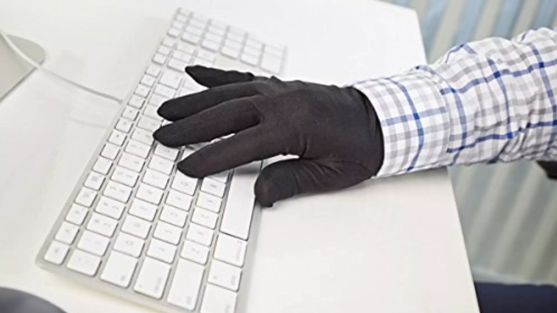 Tangan seseorang mengetik di keyboard sambil mengenakan sarung tangan