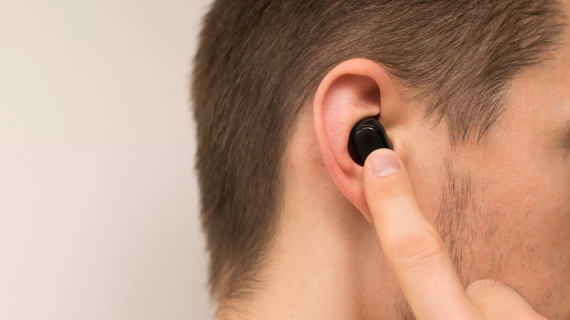 Seorang pria dengan earphone nirkabel di telinganya. Pria itu menyalakan lubang suara nirkabel dengan jarinya