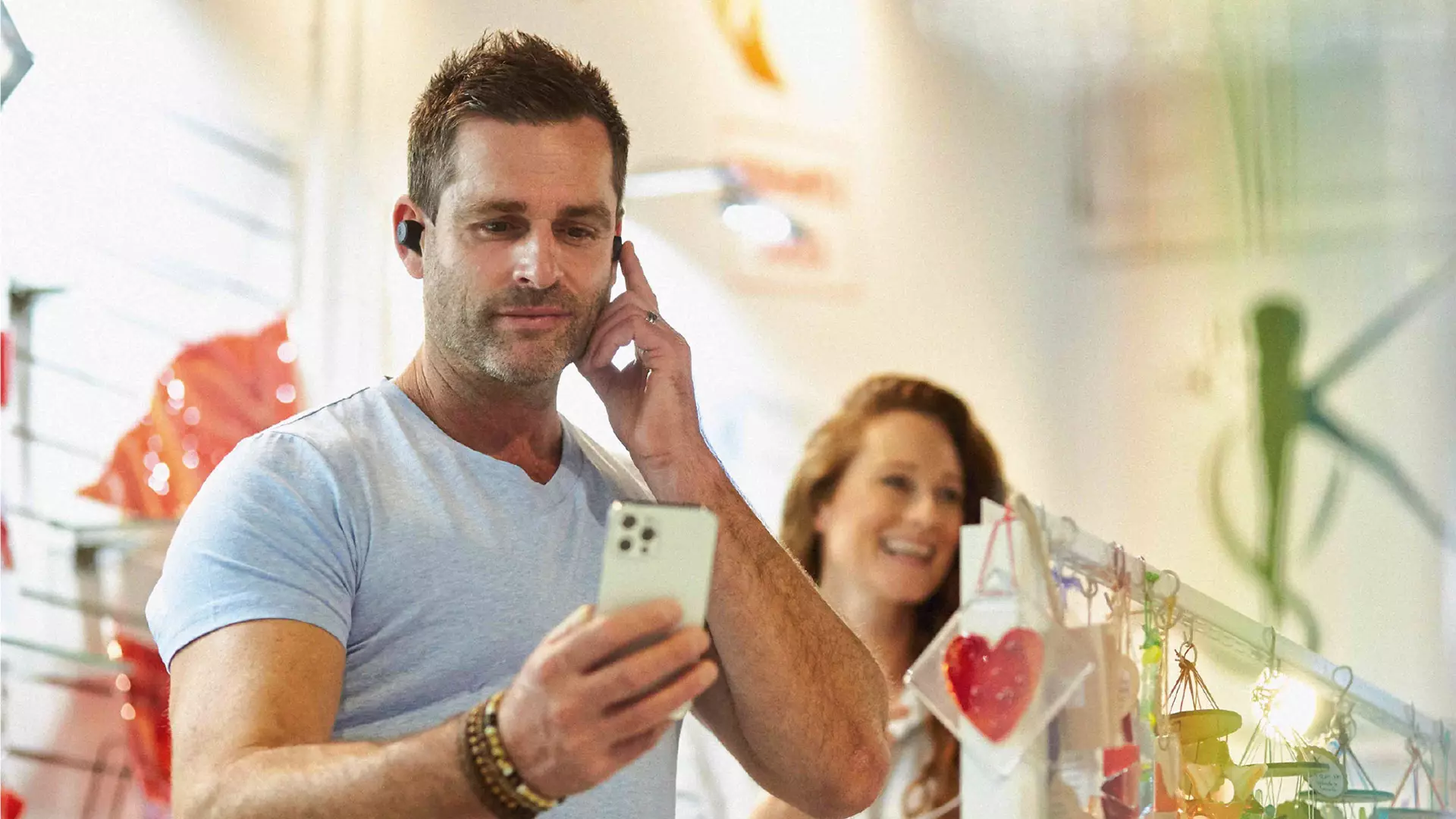 Persona que usa un audífono Nuheara y toca el audífono mientras mira su teléfono inteligente