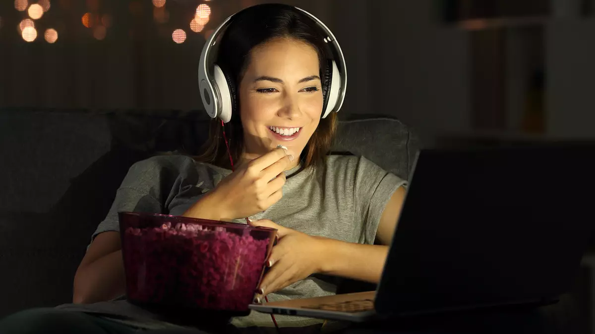 O fată care mănâncă floricele de porumb în timp ce discută video și se uită la Netflix cu prietenii.