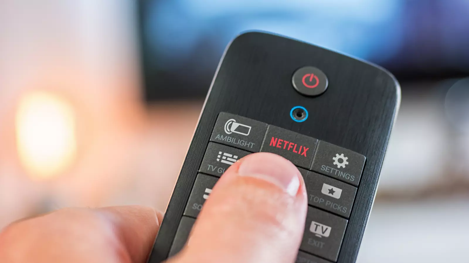 Човек държи дистанционно управление и натиска бутон Netflix върху него