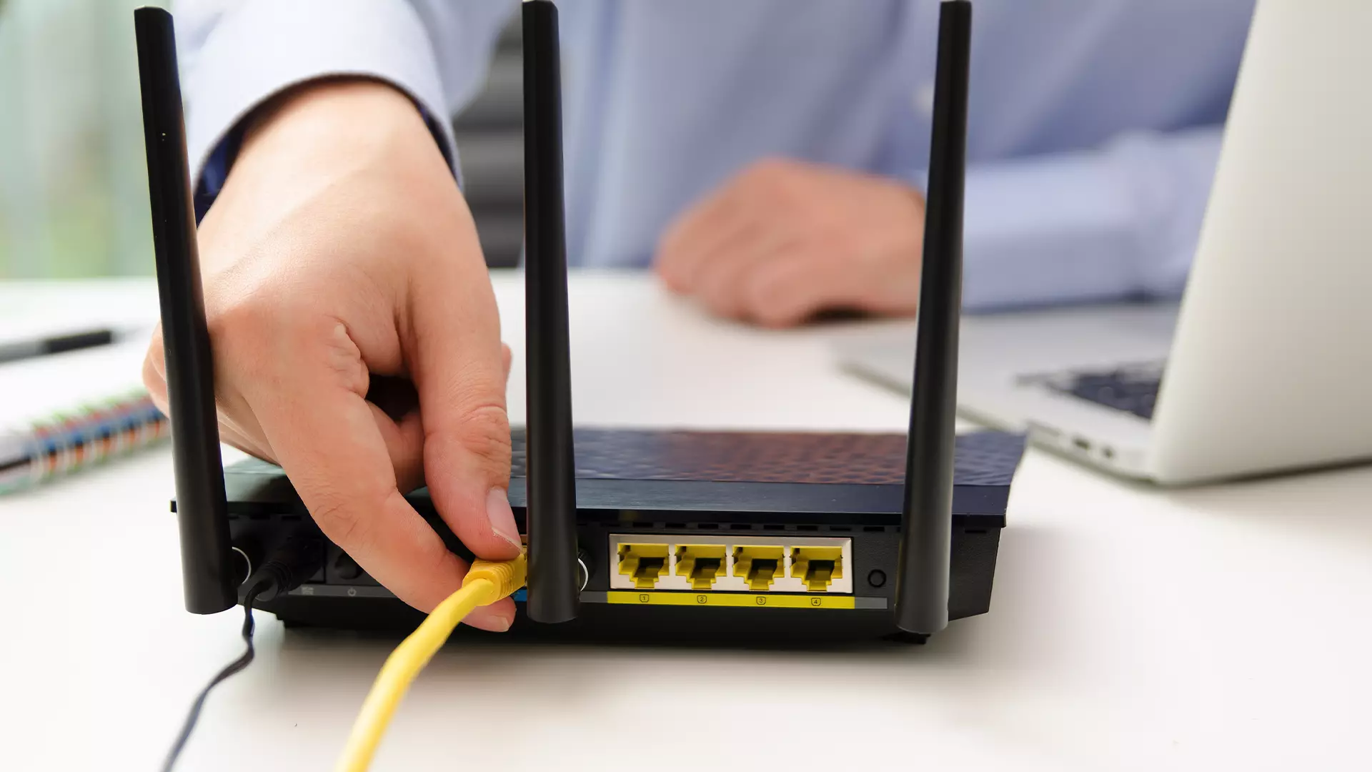 Dikush që lidh një kabllo Ethernet në pjesën e pasme të një ruteri Wi-Fi.