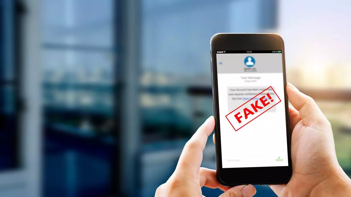Homme tenant un téléphone montrant un faux message texte frauduleux