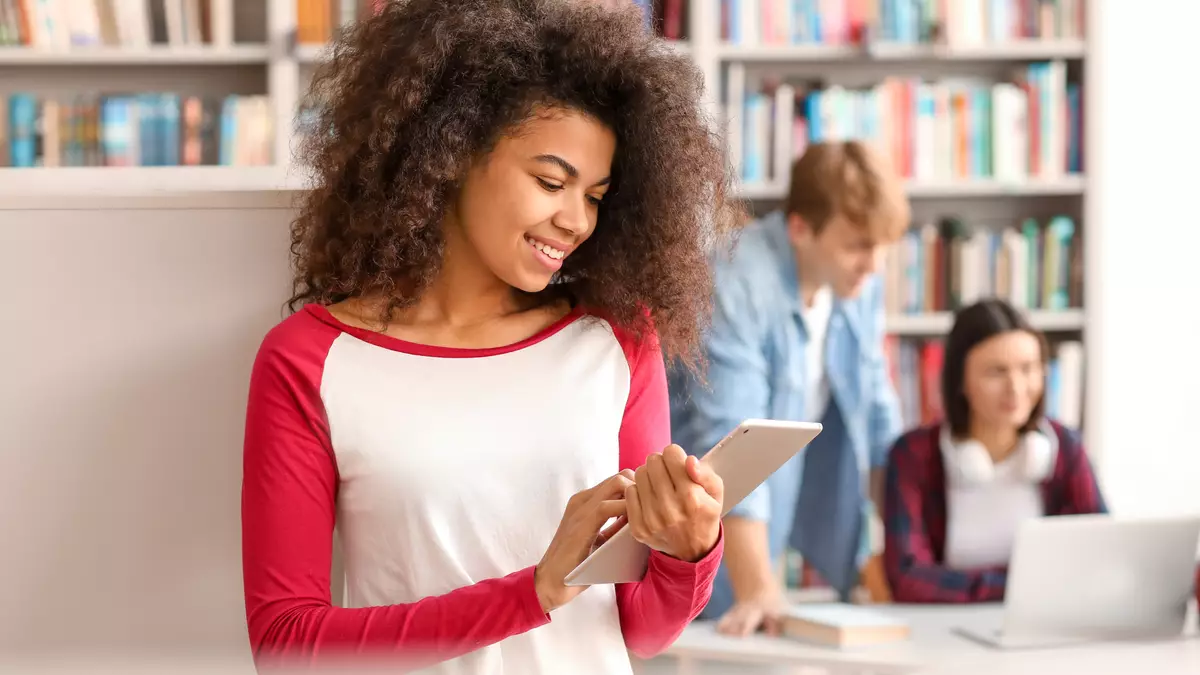 Jongeren in een bibliotheek kijken naar boeken en films op tablet en laptop