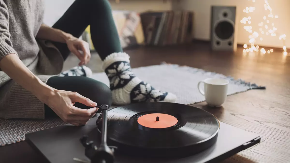 Kvinna som lyssnar på musik, kopplar av, njuter av livet hemma. Flicka som bär varma vinterkläder som har roligt. Skivspelare som spelar vinyl-LP-skiva.