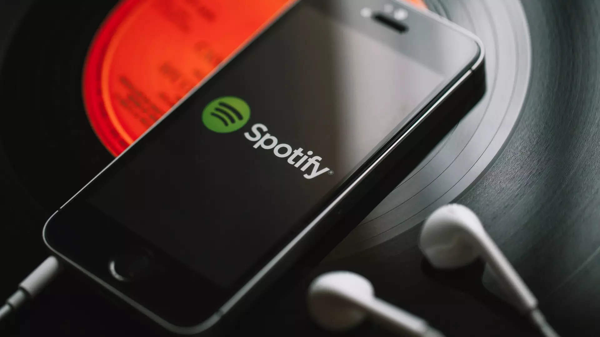Ponsel dengan layanan Spotify Music di layar dan earphone putih di piringan hitam.