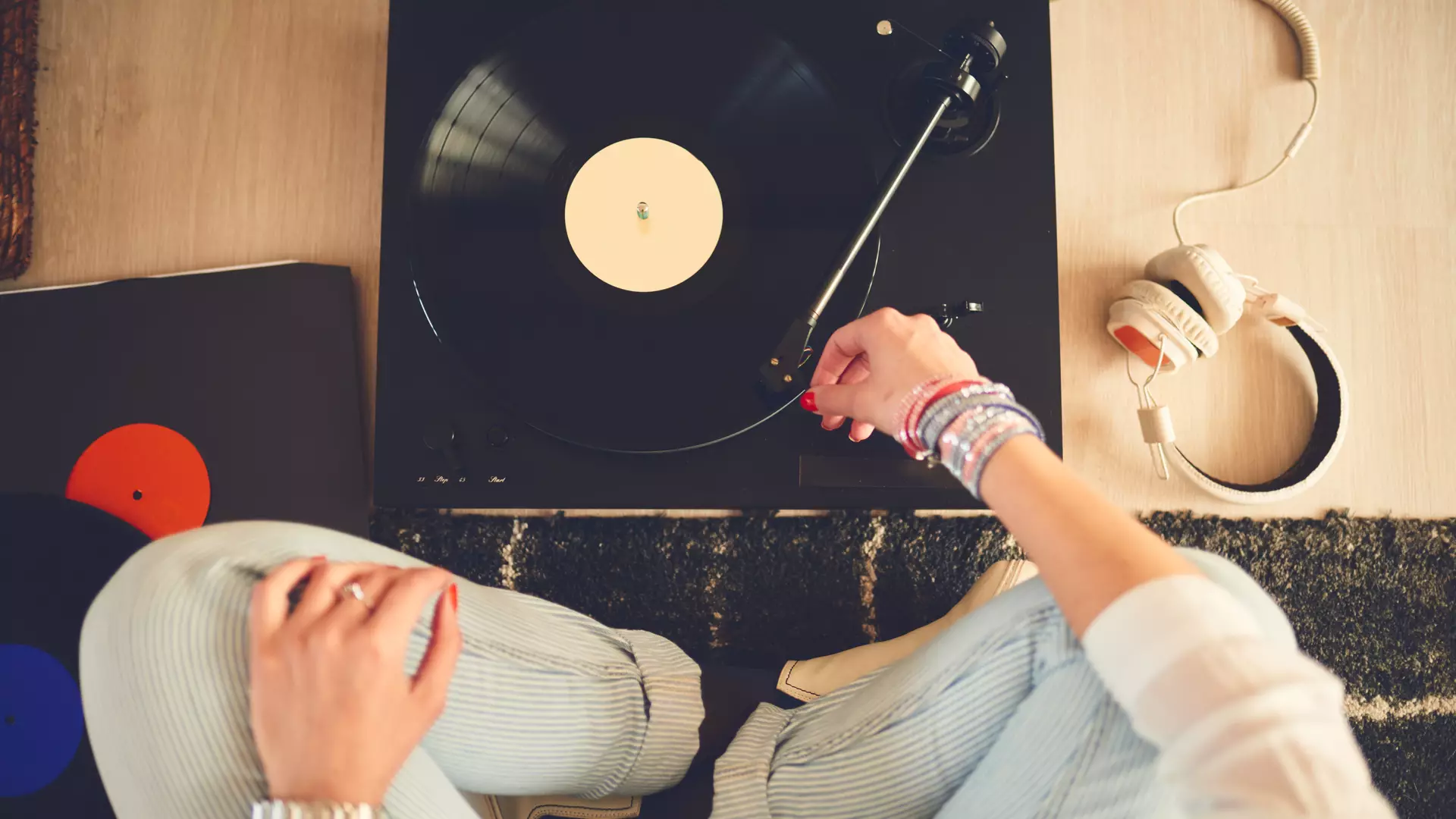 Osoba sediaca na podlahe a doma počúvajúca vinyl