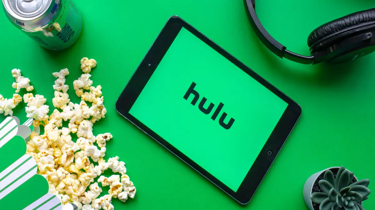 Un iPad avec le logo Hulu sur l'écran sur un fond vert avec du pop-corn et des écouteurs