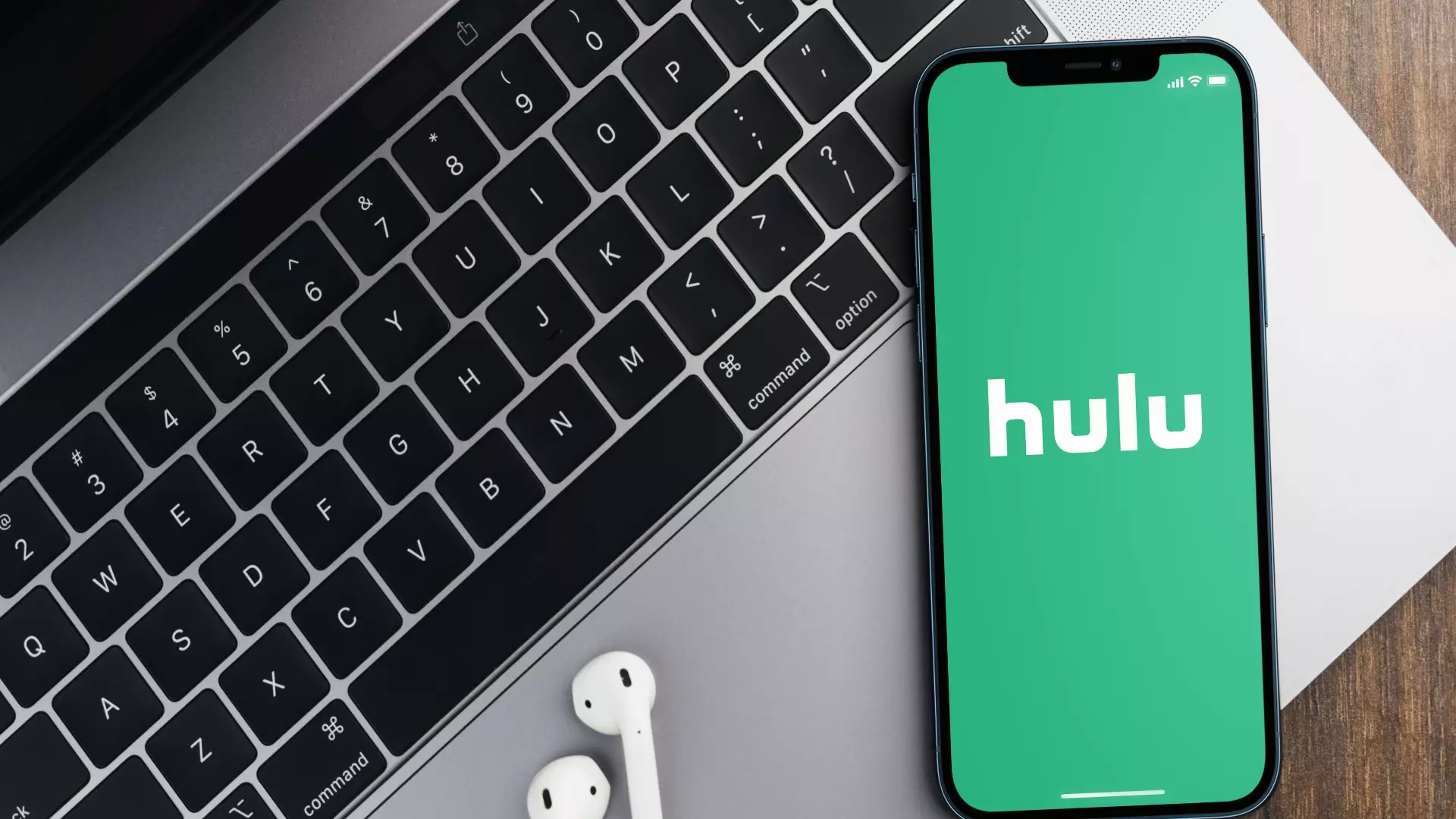 သစ်သားနောက်ခံတွင် စမတ်ဖုန်းစခရင်ပေါ်ရှိ Hulu အက်ပ်ကို ၎င်းဘေးရှိ ကွန်ပျူတာဖြင့် ပြုလုပ်ထားသည်။ ထိပ်တန်းမြင်ကွင်း။