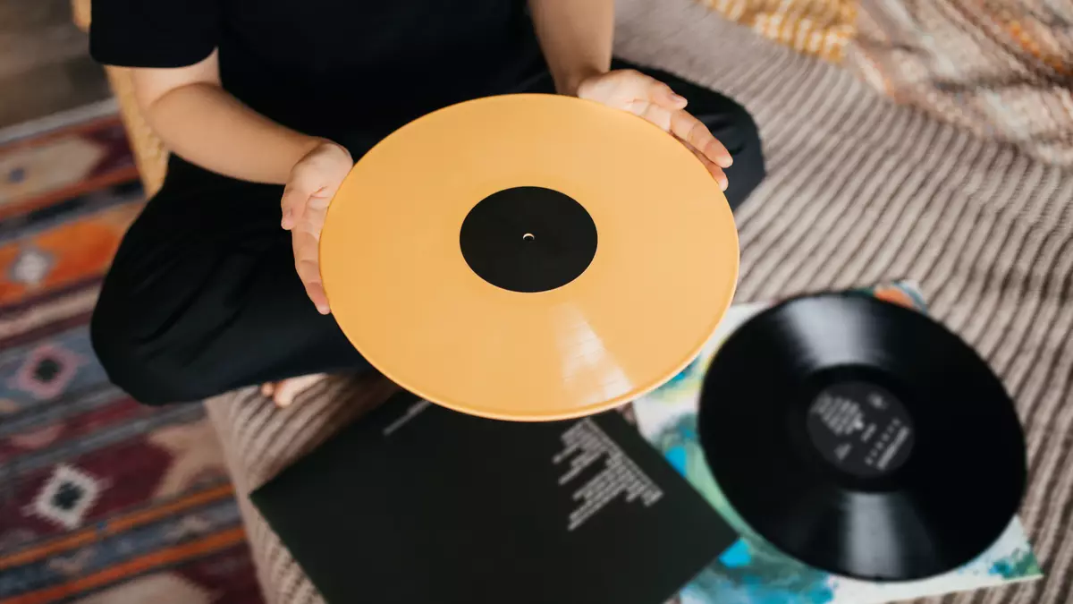 विंटेज विनाइल रिकॉर्ड से सजी काली दीवार वाले कमरे में पीले विलील रिकॉर्ड रखने वाली युवती। विंटेज और रेट्रो शैली।