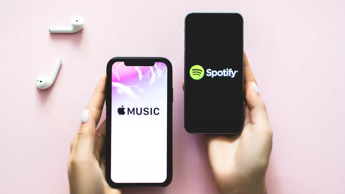 ръце, държащи iPhone X с приложението Apple Music и друг с услуги за стрийминг на музика Spotify