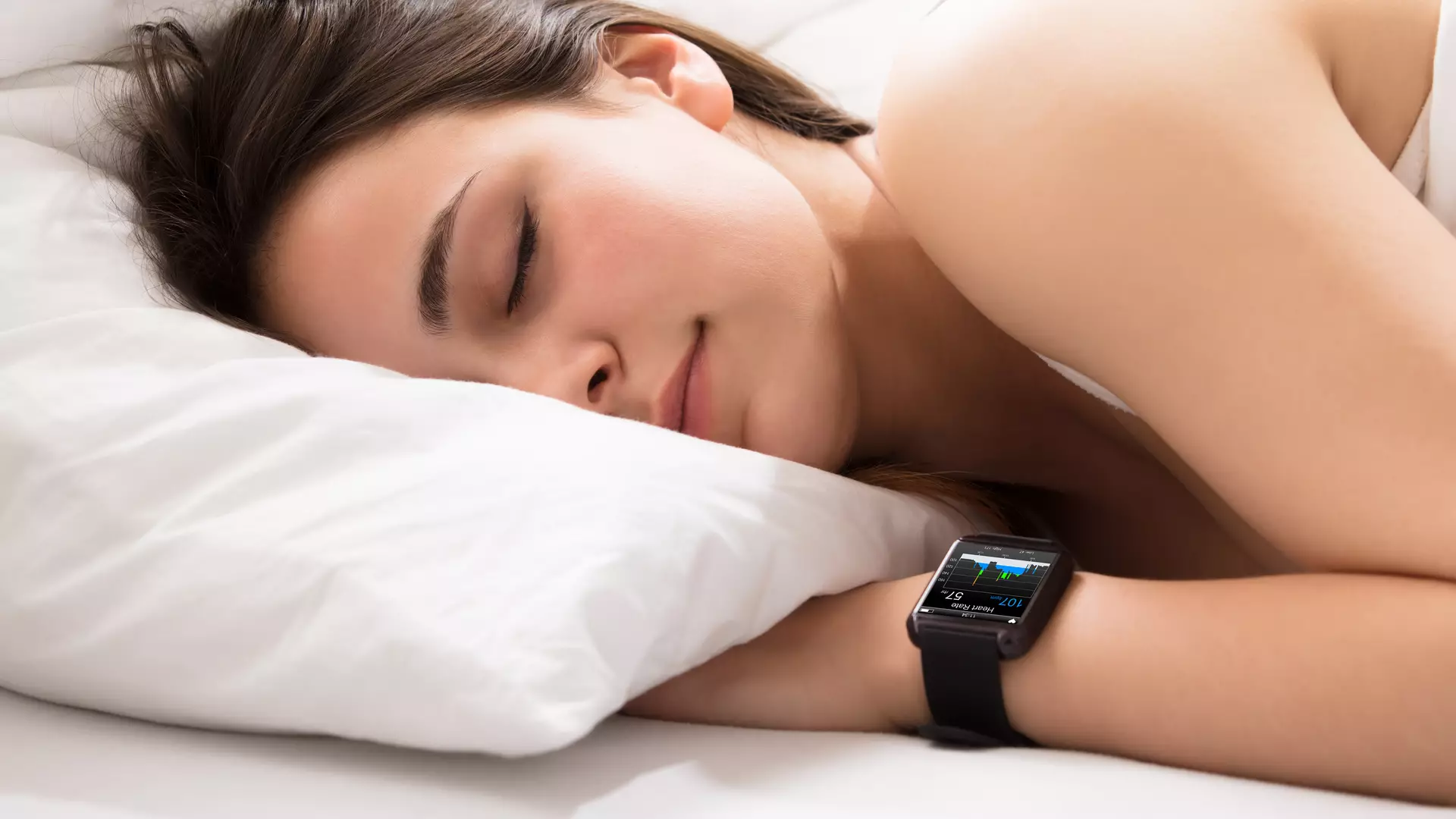 Oseba, ki spi na postelji s pametno uro, ki prikazuje monitor srčnega utripa