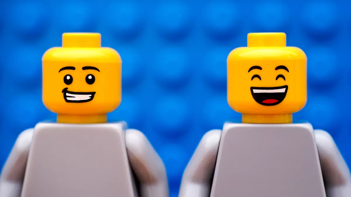 Dua patung kecil Lego - satu dengan senyuman dan seorang gembira. Latar belakang biru. Gambar studio.