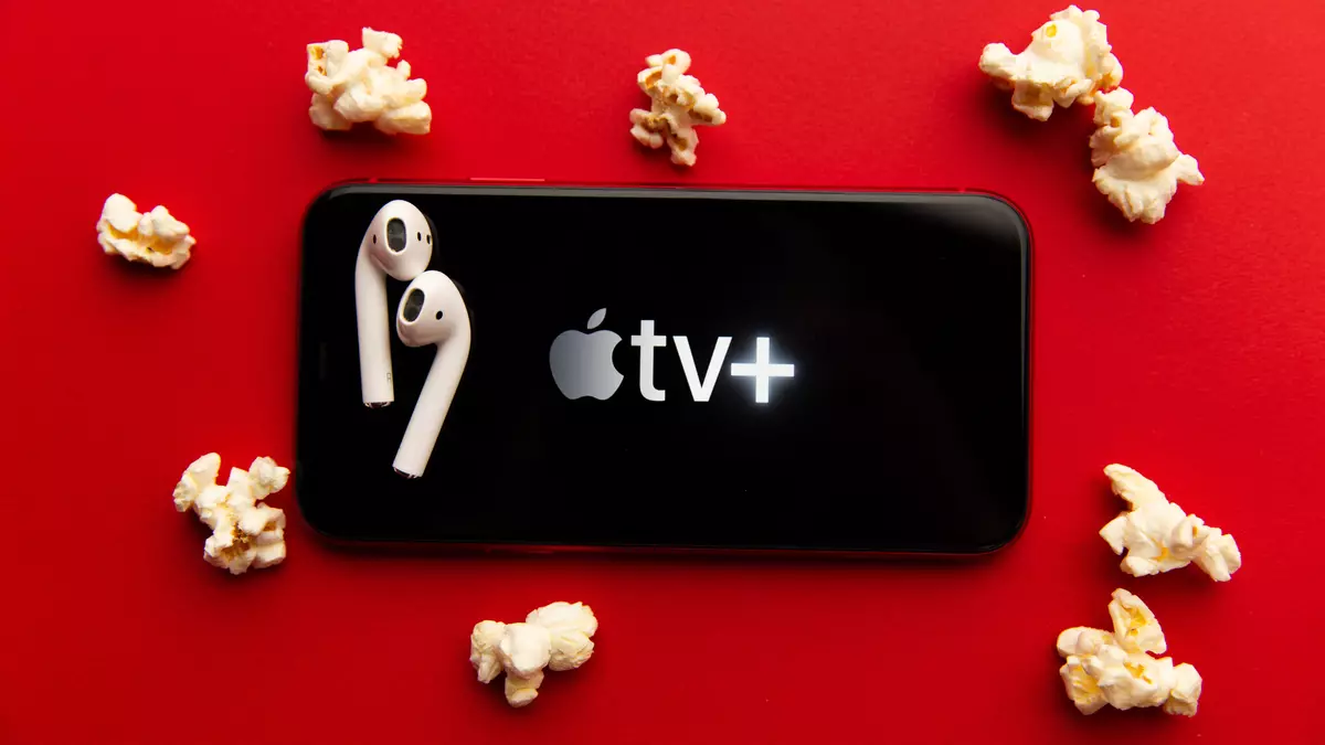 ໂລໂກ້ Apple TV Plus ໃນ iPhone ສະແດງຢູ່ພື້ນຫຼັງສີແດງພ້ອມປັອບຄອນ