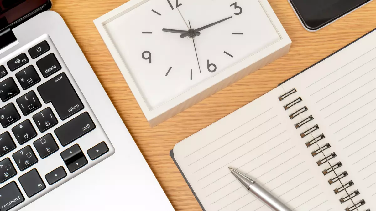 Conceptul de management al timpului, cu o privire de sus în jos asupra unui ceas, laptop, smartphone, notebook și stilou.