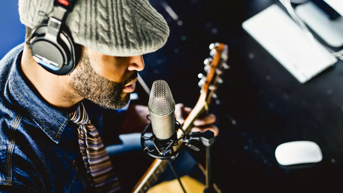 Nhạc sĩ ghi âm tại nhà chơi guitar và hát vào micrô khi bật tai nghe