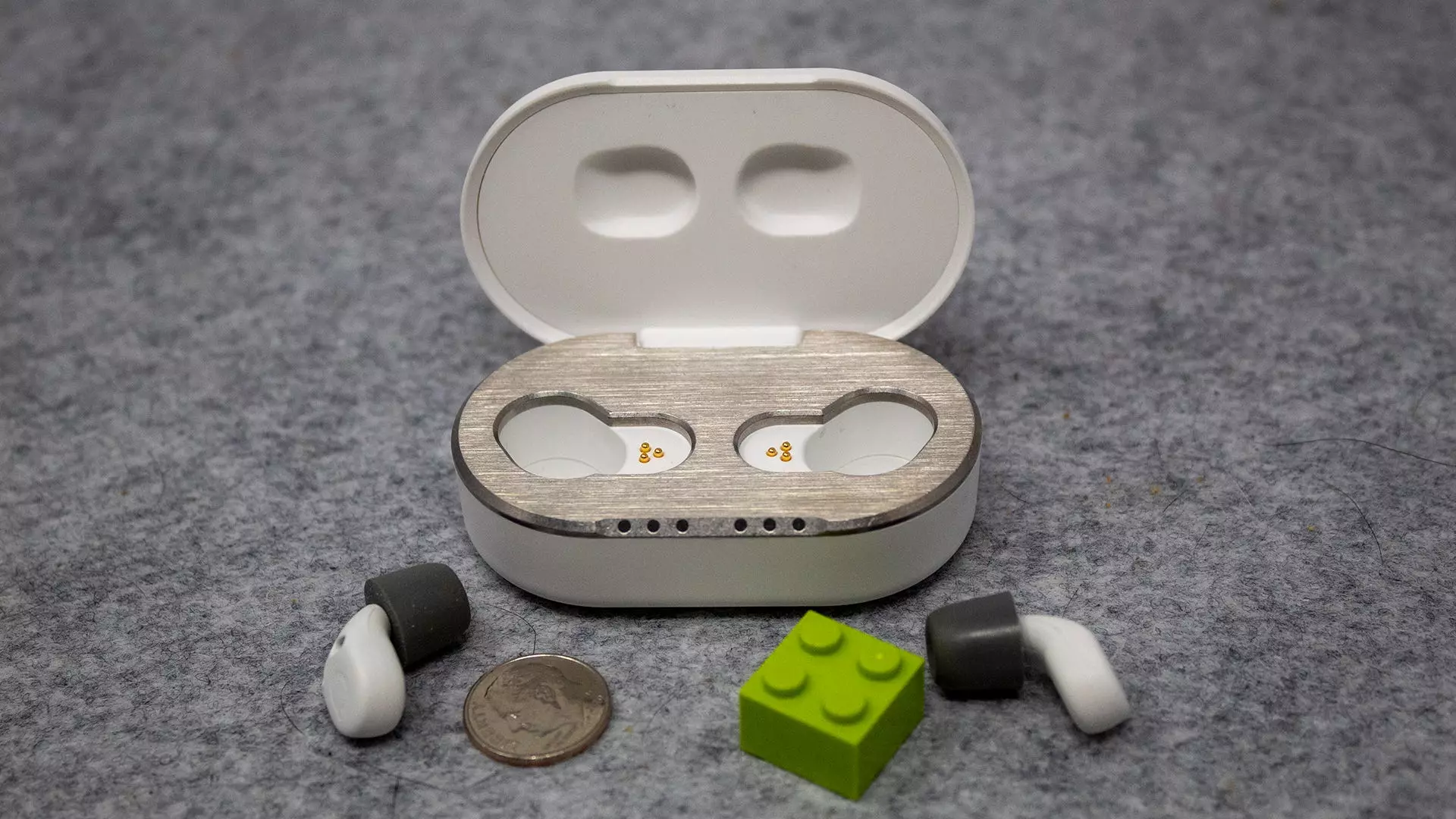 Um minúsculo fone de ouvido ao lado de uma moeda de dez centavos quase do mesmo tamanho e LEGO