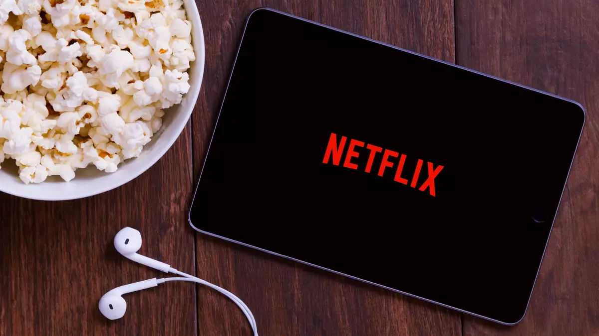 Sto s bocom kokica i Netflix logom na Apple Ipad mini i slušalicama. Netflix je globalni provajder za streaming filmova i TV serija.