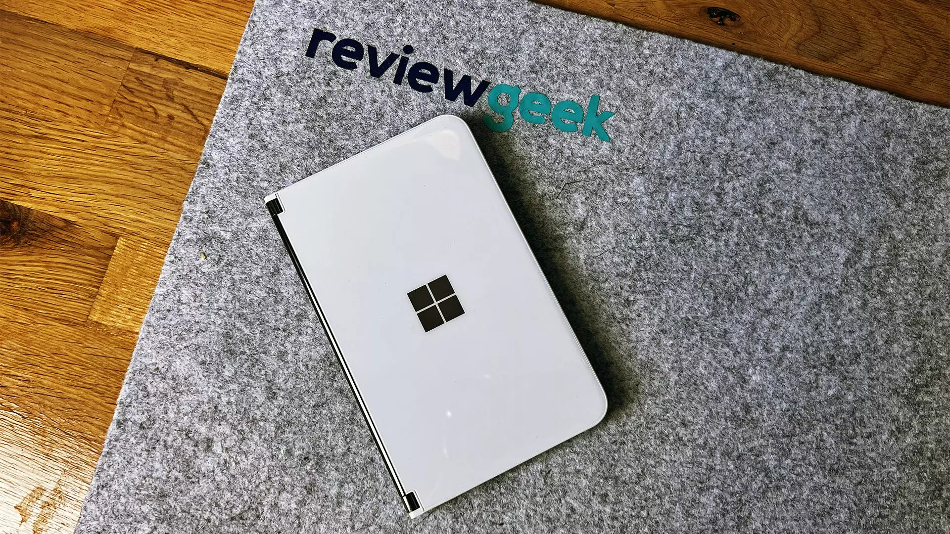 Un Surface Duo 2 închis pe un covoraș cu sigla Review Geek