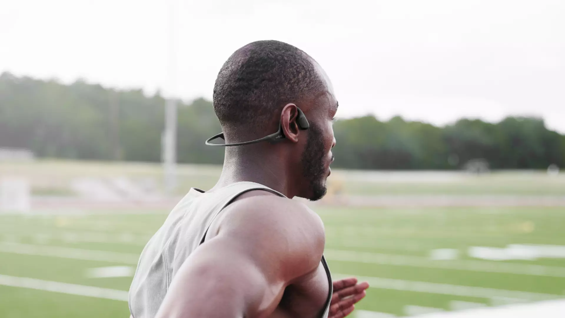 ספורטאי שלובש את Shokz OpenRun Pro עצם מוליכת אוזניות בזמן ריצה במסלול חיצוני