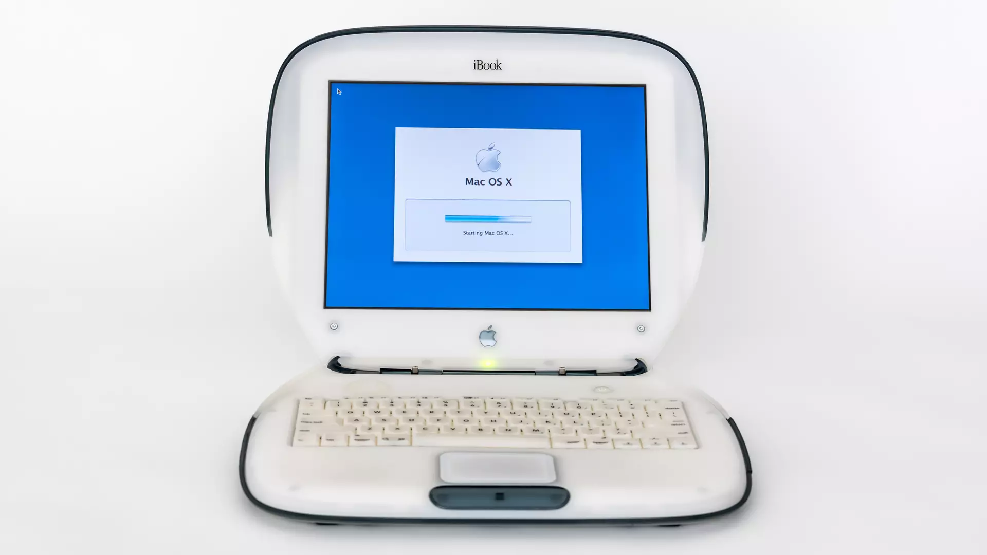 Mac OS X പ്രദർശിപ്പിക്കുന്ന സ്റ്റാർട്ടപ്പ് സ്ക്രീനോടുകൂടിയ പഴയ ആപ്പിൾ ക്ലാംഷെൽ ശൈലിയിലുള്ള iBook ലാപ്ടോപ്പ് കമ്പ്യൂട്ടർ