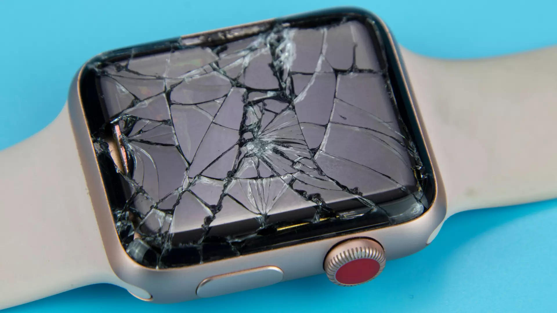 La pantalla del Apple Watch se agrietó de color rosa en el suelo y espera ser reparada. Sobre fondo azul.