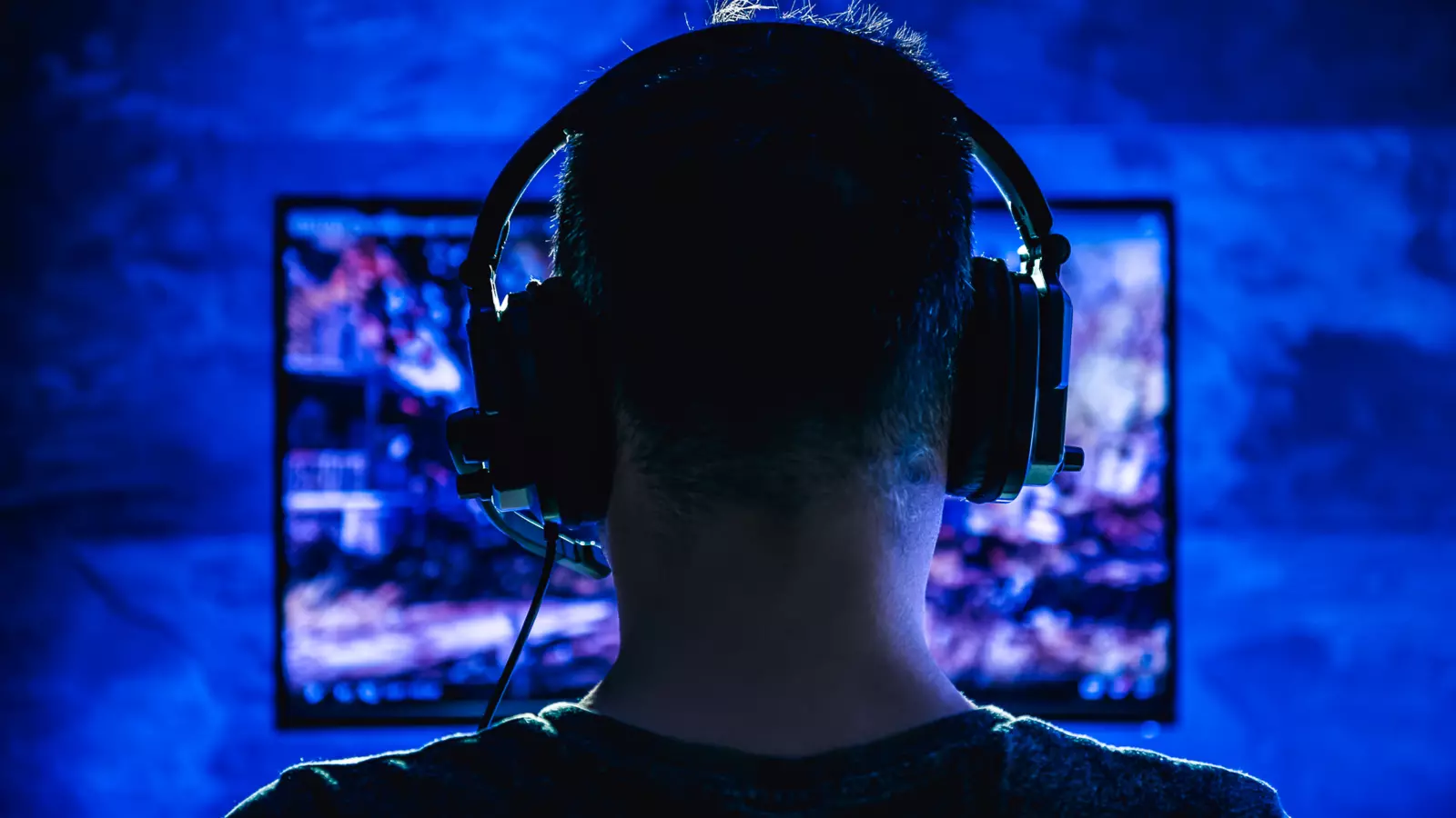 คนใส่หูฟังเล่นเกมในทีวีในห้องมืดที่มีไฟสีฟ้า