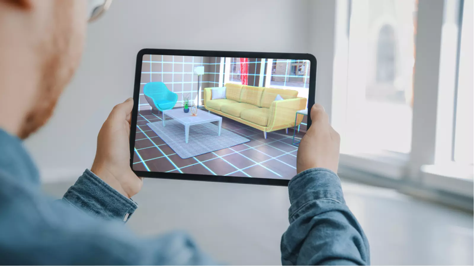 Человек, держащий цифровой планшет с открытым приложением для дизайна интерьера с дополненной реальностью, виртуально примеряя мебель в комнате