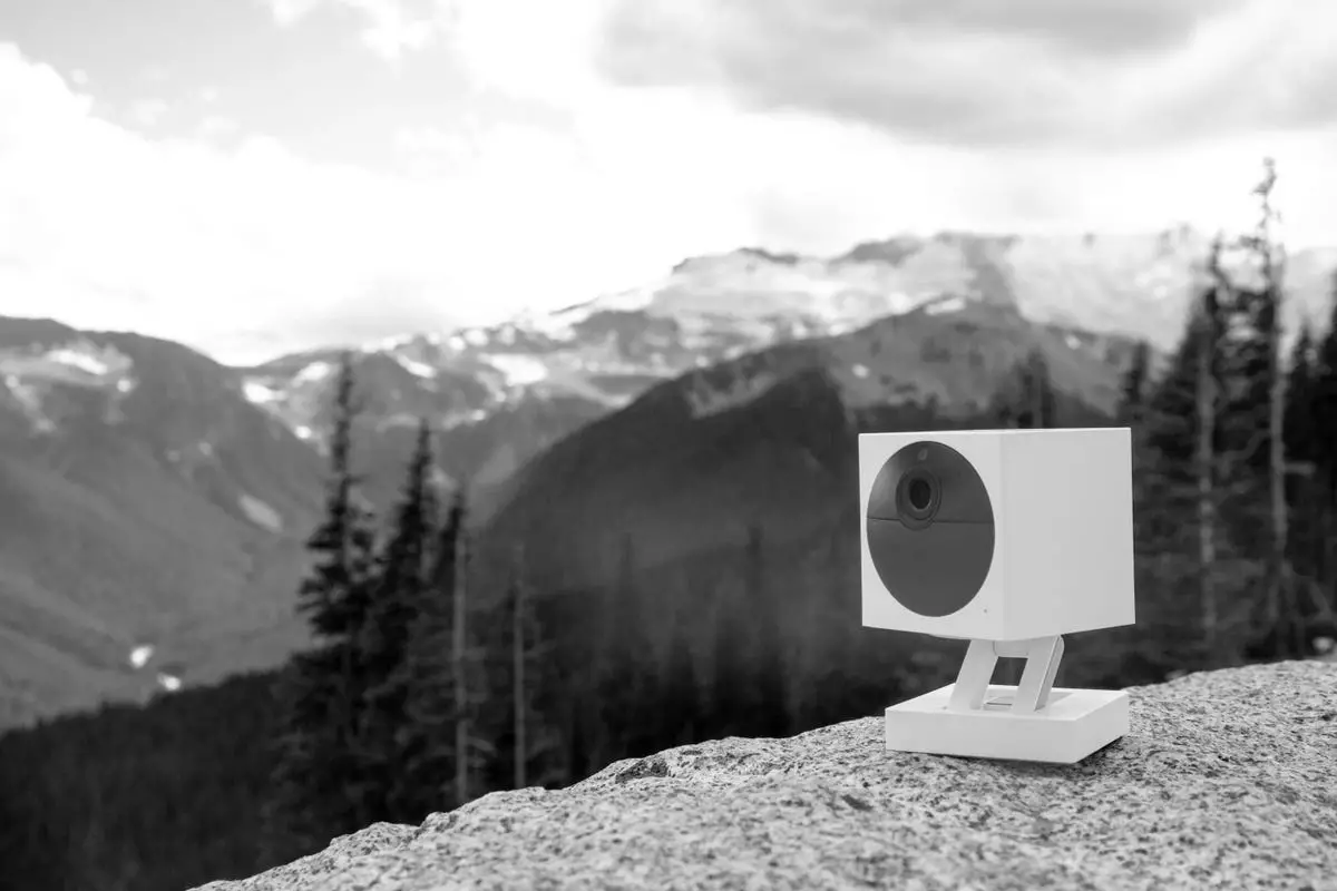 Uma foto em preto e branco de um modelo Wyze Cam Outdoor em uma área montanhosa.