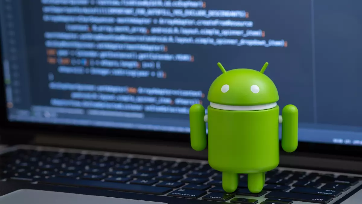 Фігурка Google Android, якая стаіць на клавіятуры ноўтбука з кодам у фонавым рэжыме
