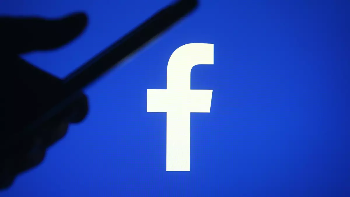 Logo Facebook kanthi silohette tangan nggunakake smartphone.