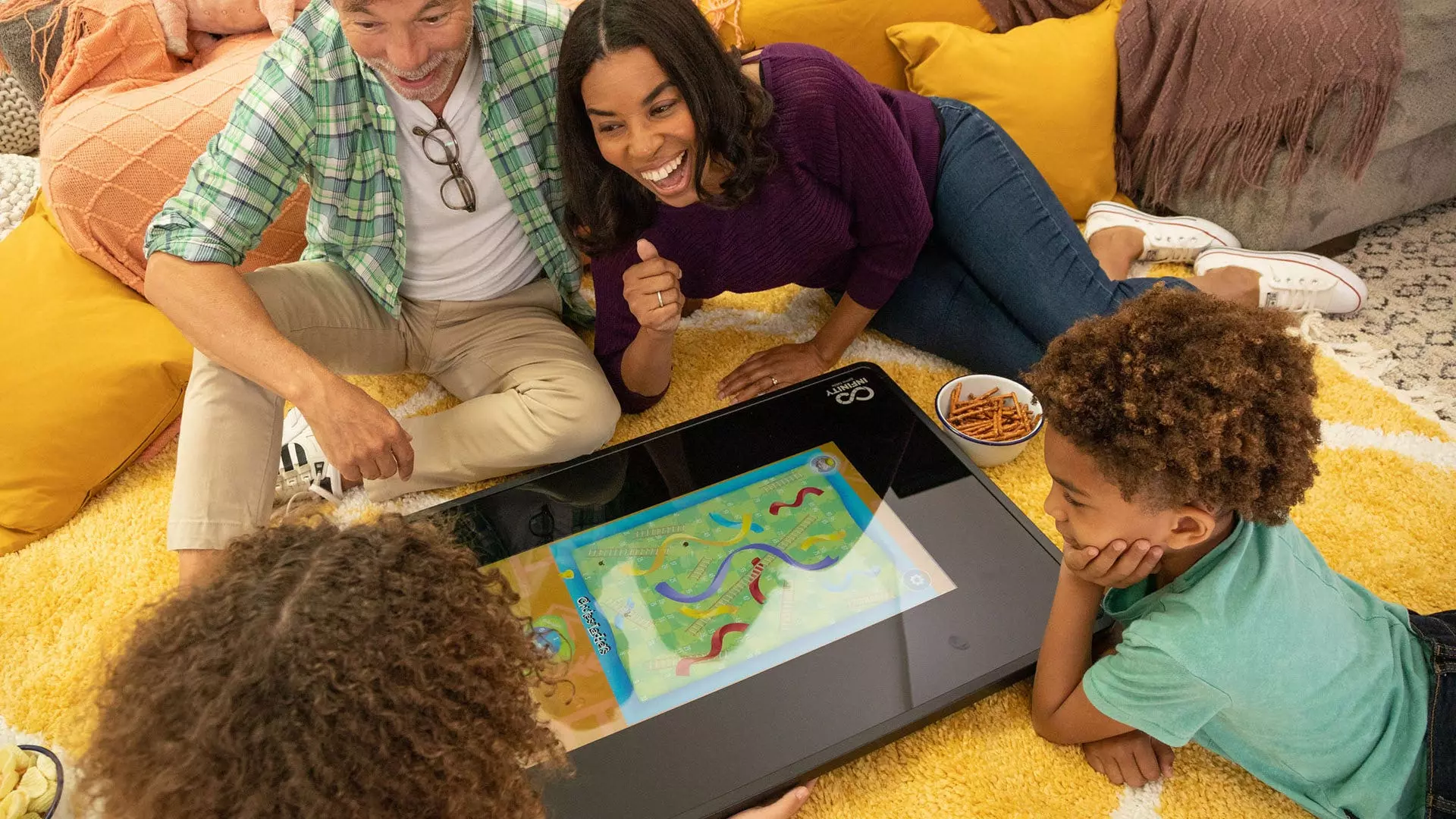 Četiri osobe igraju igru 'Chutes and Ladders' na podu s digitalnim stolom za društvene igre.