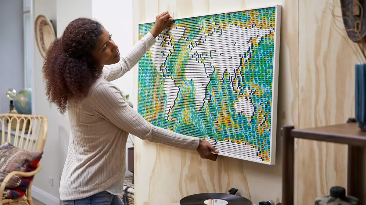 Persoon wat hul voltooide LEGO Art World Map-stel teen die muur monteer in 'n kamer met wêreldse versierings