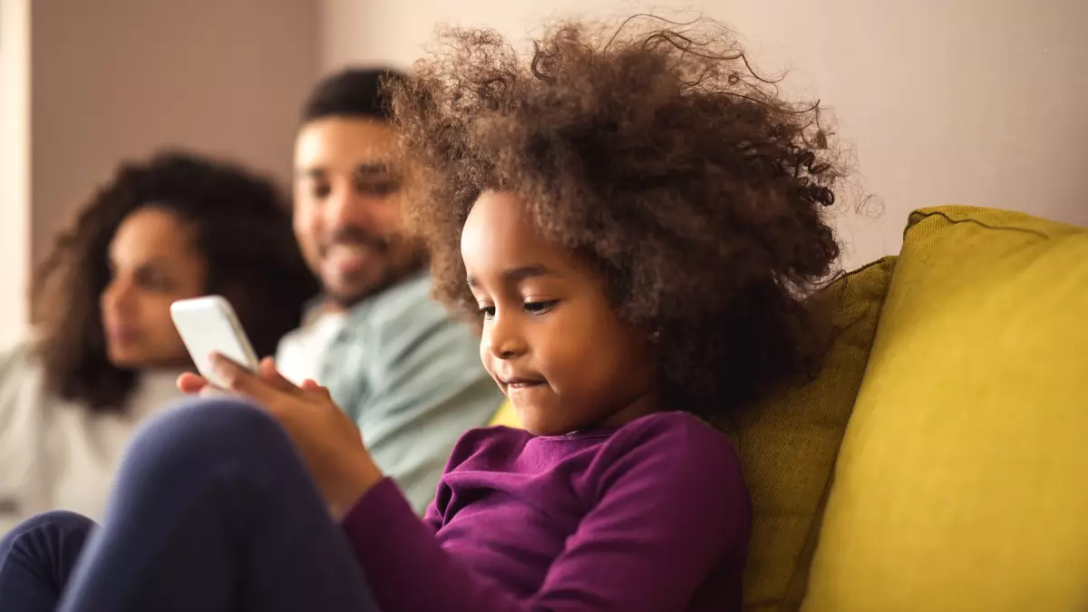 Niño lindo mirando el teléfono inteligente mientras se sienta junto a los padres en el sofá