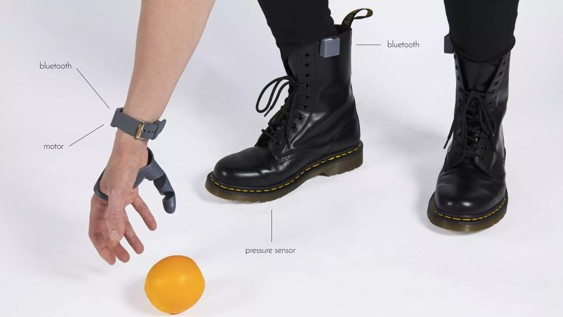 Čovjek koji s dva palca poseže za narančom i bežični senzori povezani s njegovim čizmama.