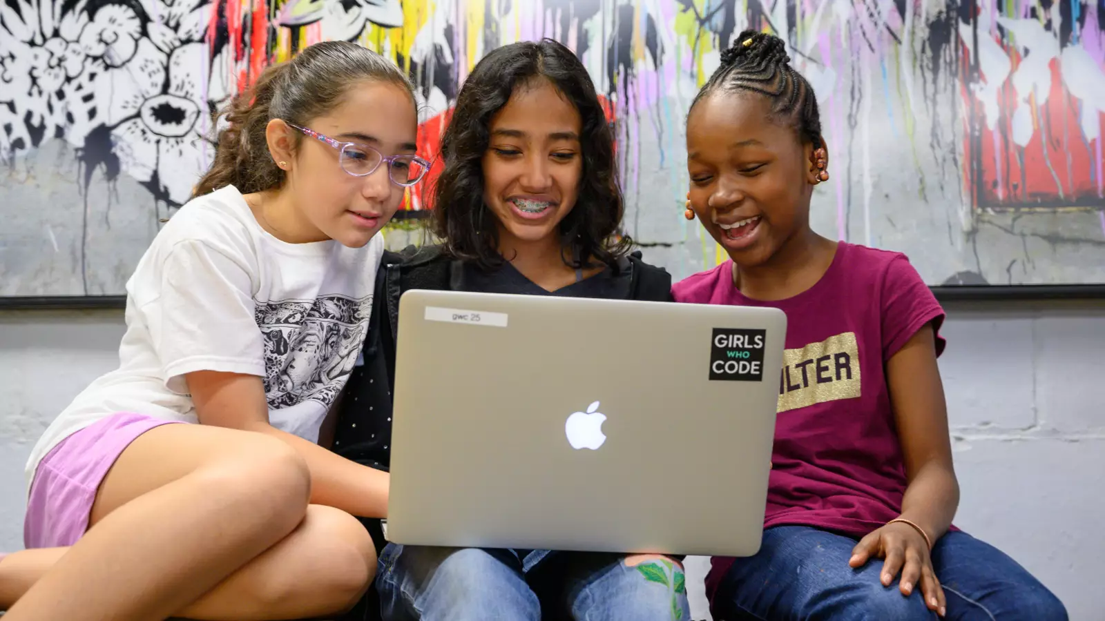 तीन लड़कियां कंप्यूटर कोड देख रही हैं और मुस्कुरा रही हैं