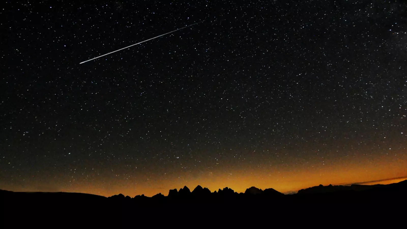 Sterren aan de nachtelijke hemel boven bergsilhouet met meteorenregen