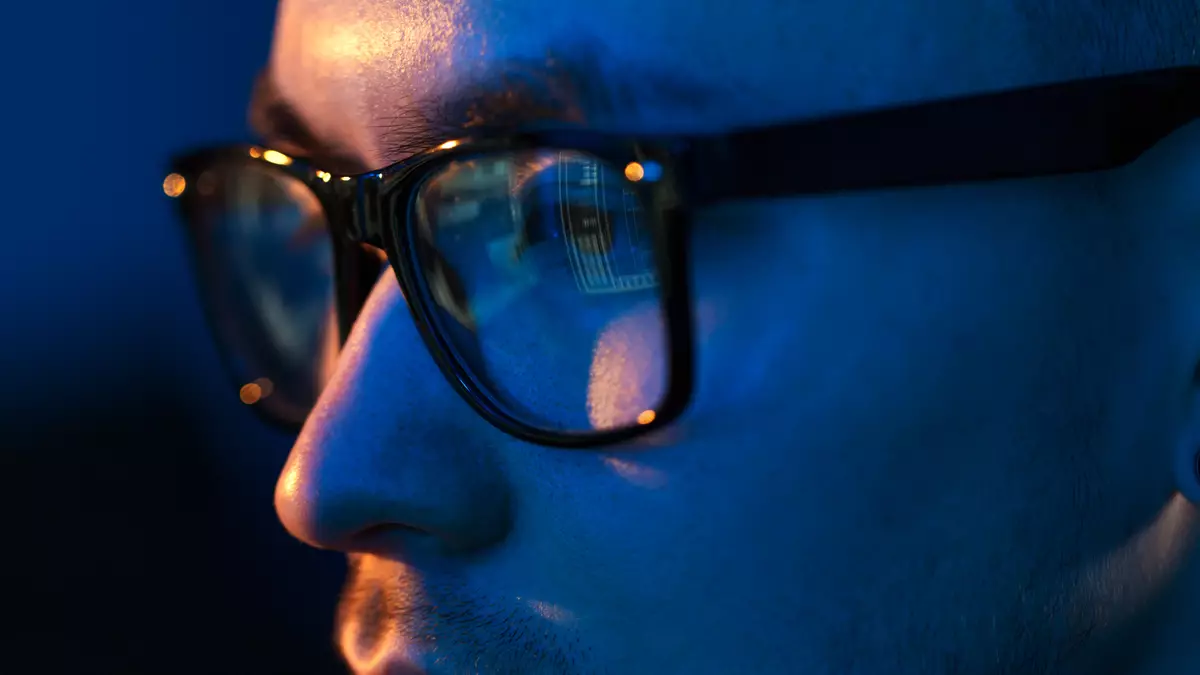 Primul plan al unei persoane care poartă ochelari de vedere care se uită la ecranul unui computer în întuneric