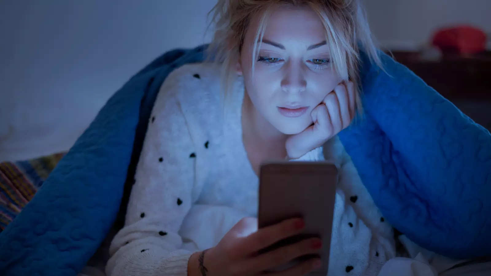 Человек, держащий мобильный телефон, сидя на кровати ночью