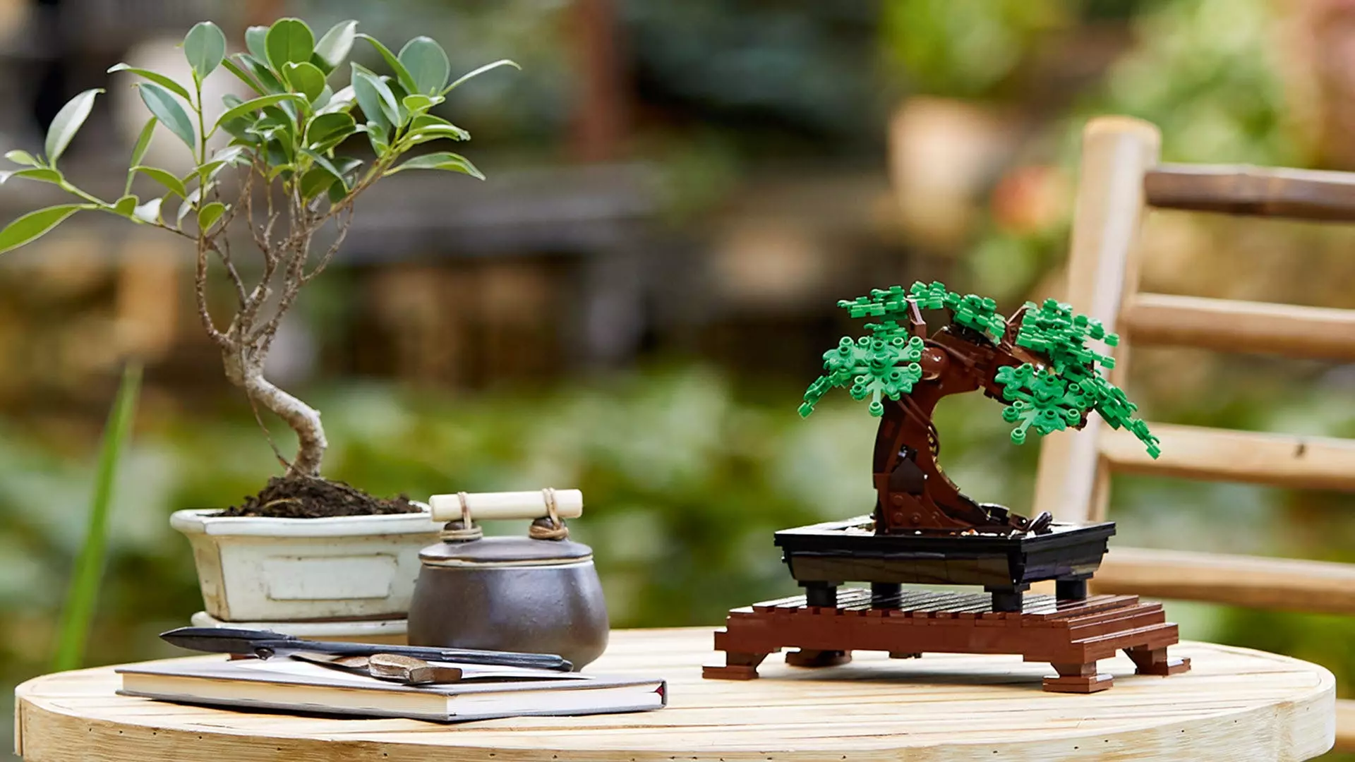 Дерево бонсай Lego на столе с другим растением, книгой и разными предметами.