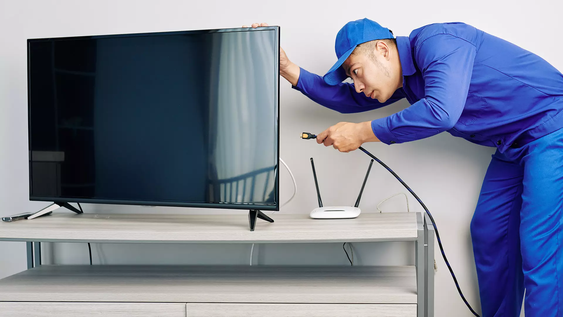 Kabloteknikisto ŝtopanta samaksan kablon en la malantaŭon de platekrana televidilo.