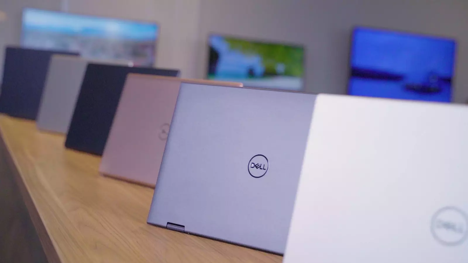 Noile laptopuri Dell Inspiron sprijinite în linie pe o suprafață de lemn